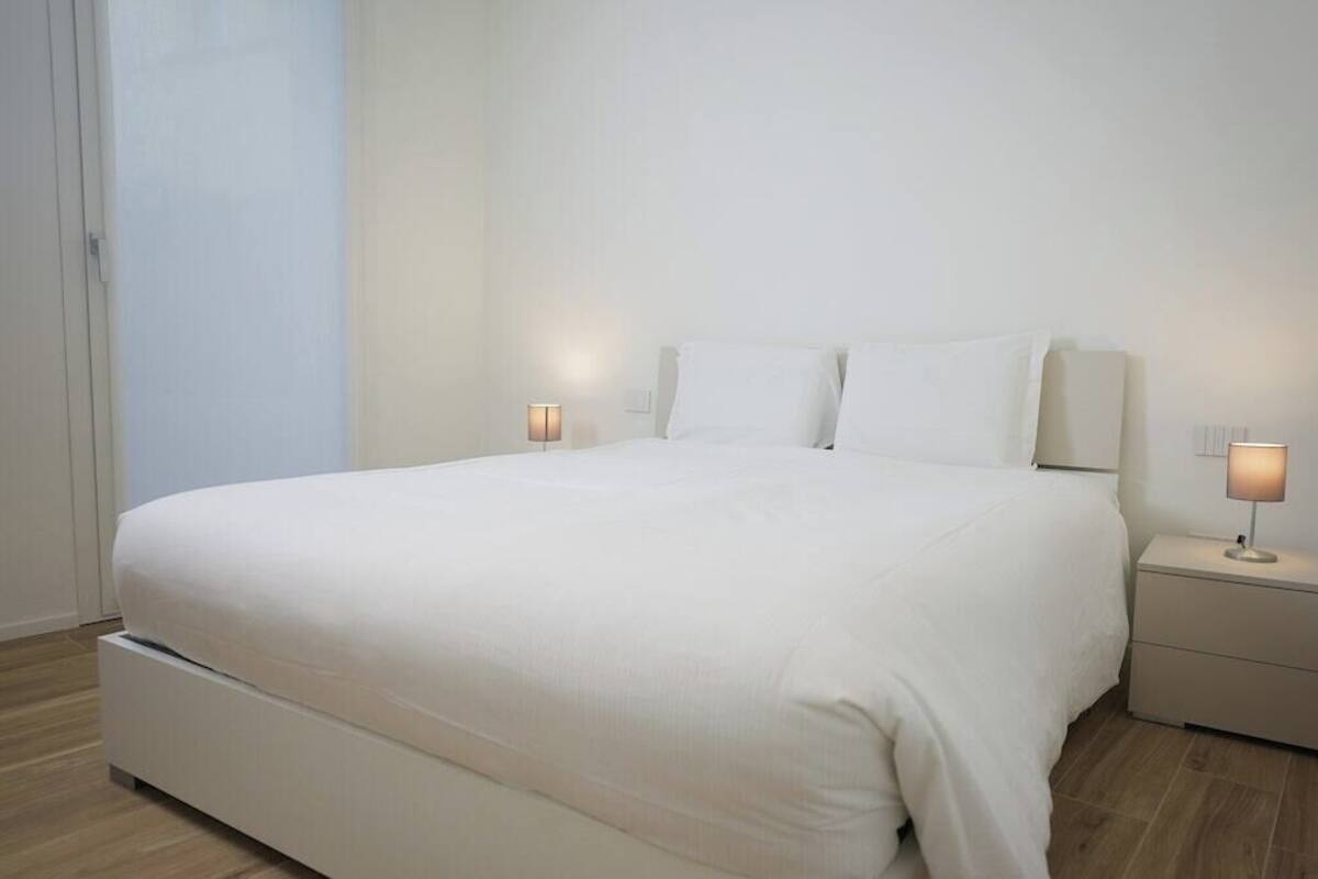 Quarto moderno com cama grande, mesas de cabeceira e uma porta.