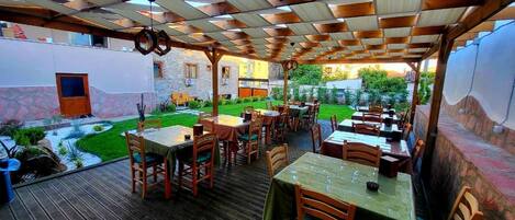 Restaurante ao ar livre com mesas e cadeiras de madeira, um deck de madeira e um jardim.