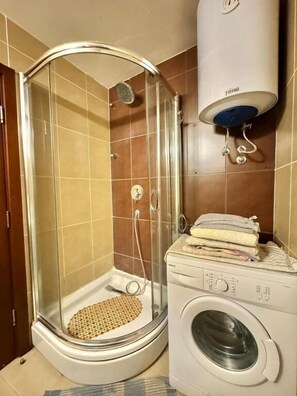 Casa de banho com cabine de duche, máquina de lavar e um porta-toalhas.