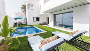 Uma área de piscina moderna ao ar livre, com espreguiçadeiras e um conjunto de jantar.