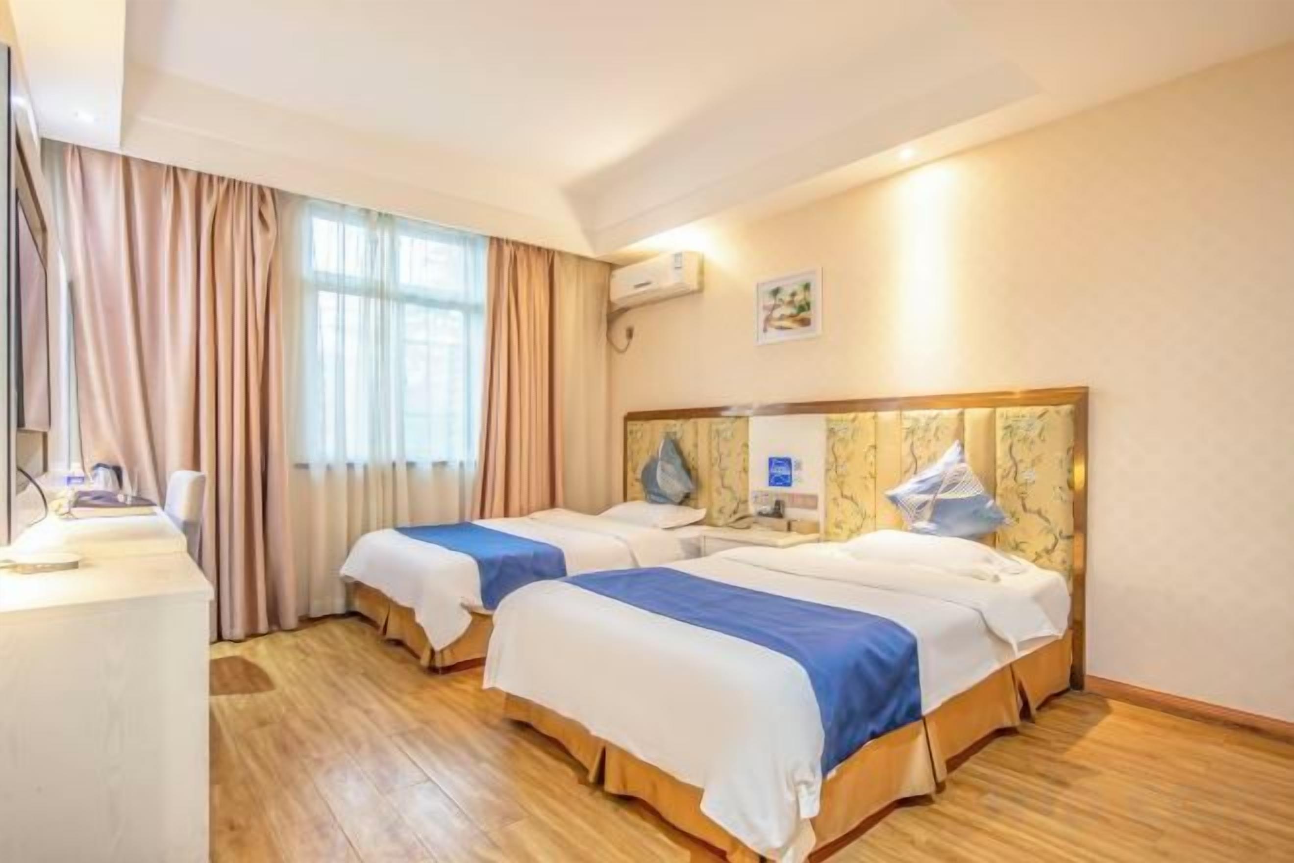 Quarto de hotel com duas camas, uma mesa e janela com cortinas.