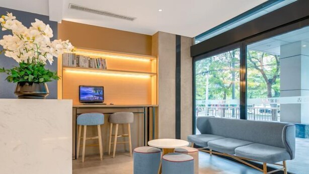 Uma área de estar moderna com um sofá, dois banquetes, uma mesa redonda e uma estante com um laptop.