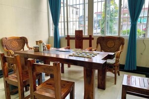 Uma mesa de jantar de madeira com cadeiras, um tabuleiro de xadrez e uma janela com cortinas.