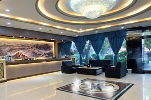 Um hall de hotel com balcão de recepção, área de estar e um lustre grande.