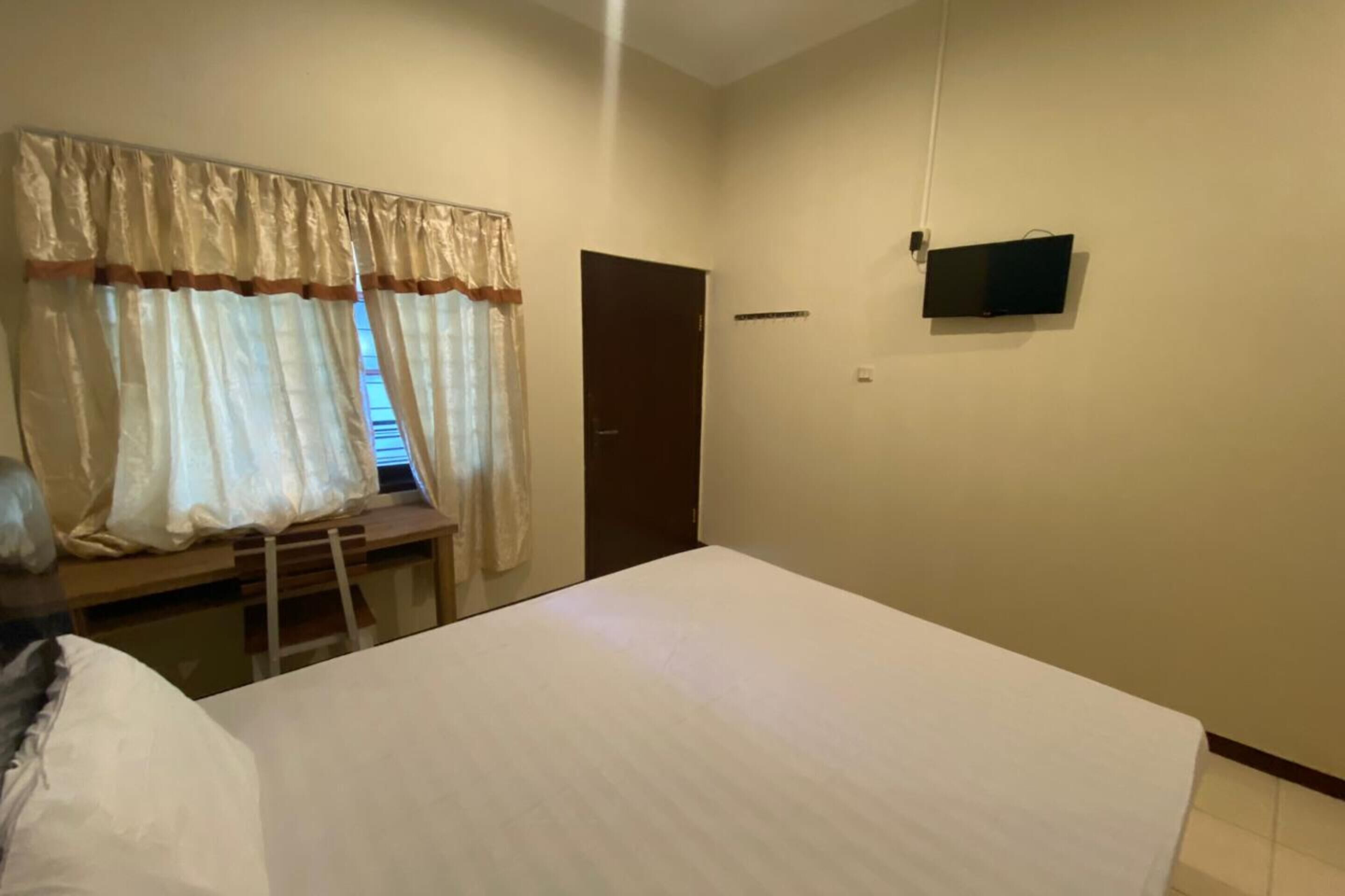 Quarto de hotel com cama, escrivaninha, cadeira, televisão na parede e porta.