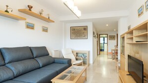 Uma sala de estar moderna com um sofá cinzento, uma mesa de centro de madeira e uma televisão sobre um suporte de madeira. Há prateleiras de madeira com objetos decorativos e um quadro na parede.