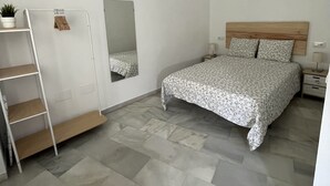 Quarto com cama, cabeceira de madeira, mesa de cabeceira, espelho, prateleira com uma planta e uma escada.