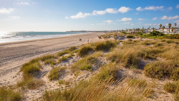 Uma praia com dunas de areia e céu claro.