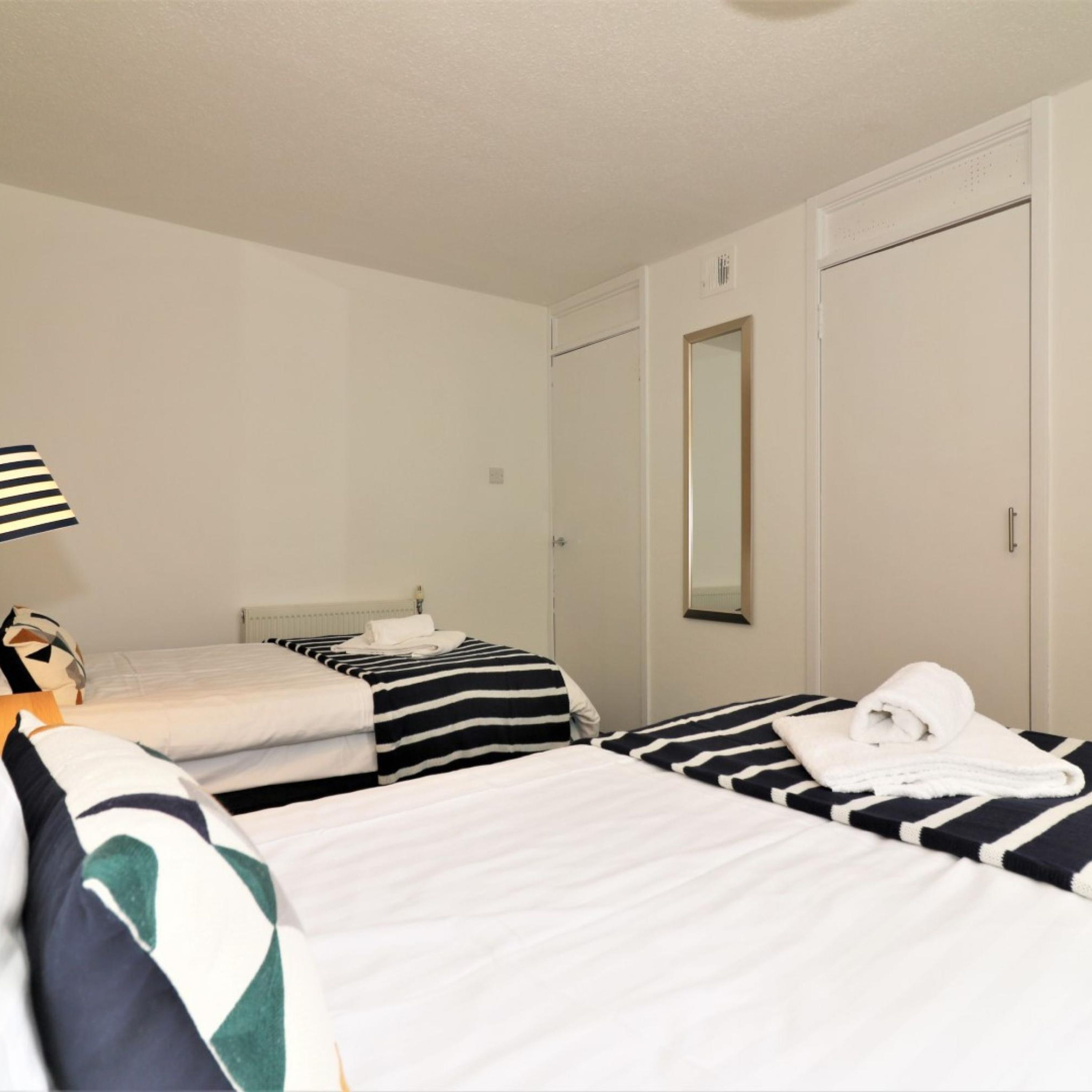 Quarto de hotel com duas camas de solteiro, um espelho grande e um guarda-roupa.