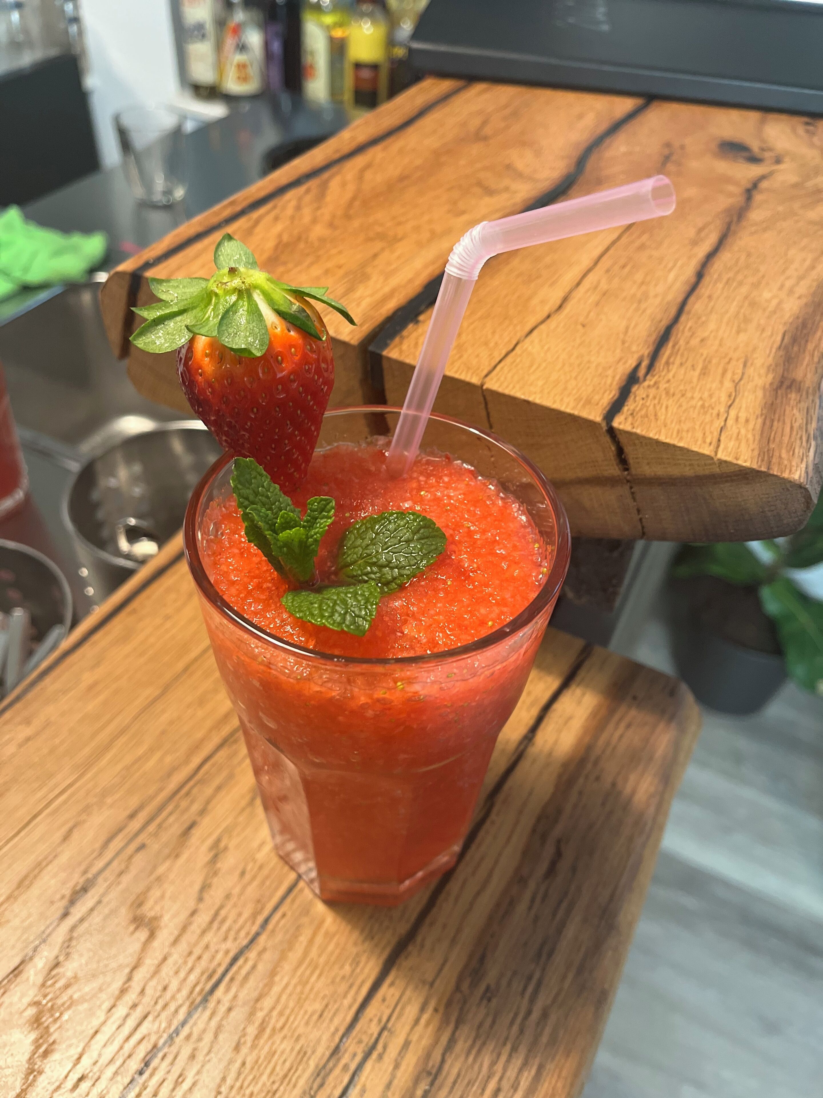 Um copo de smoothie de morango com um toque de morango e hortelã sobre uma mesa de madeira.
