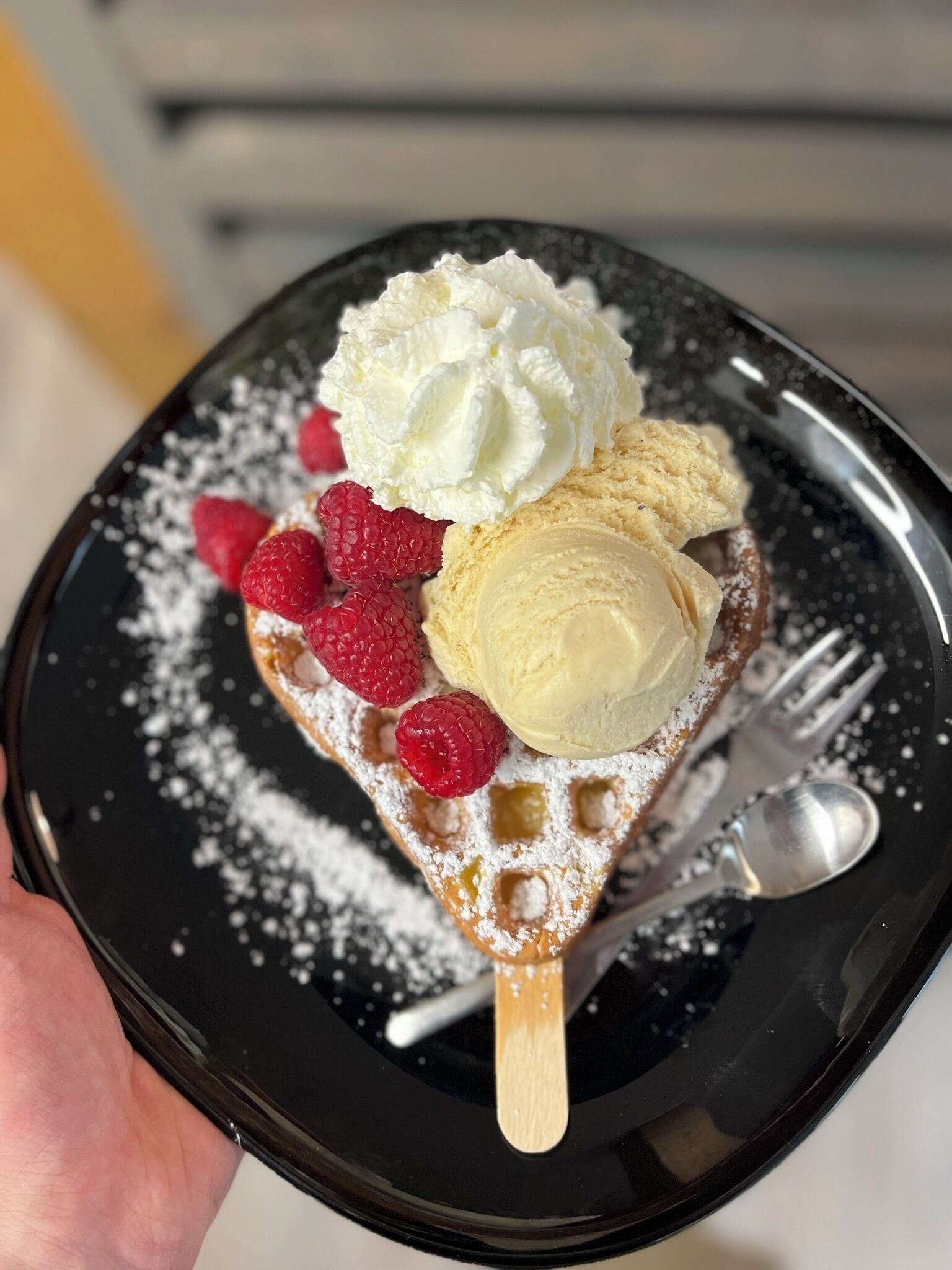 Waffle com sorvete e framboesas em um prato preto.