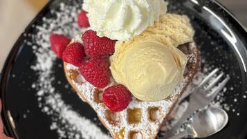 Waffle com sorvete e framboesas em um prato preto.