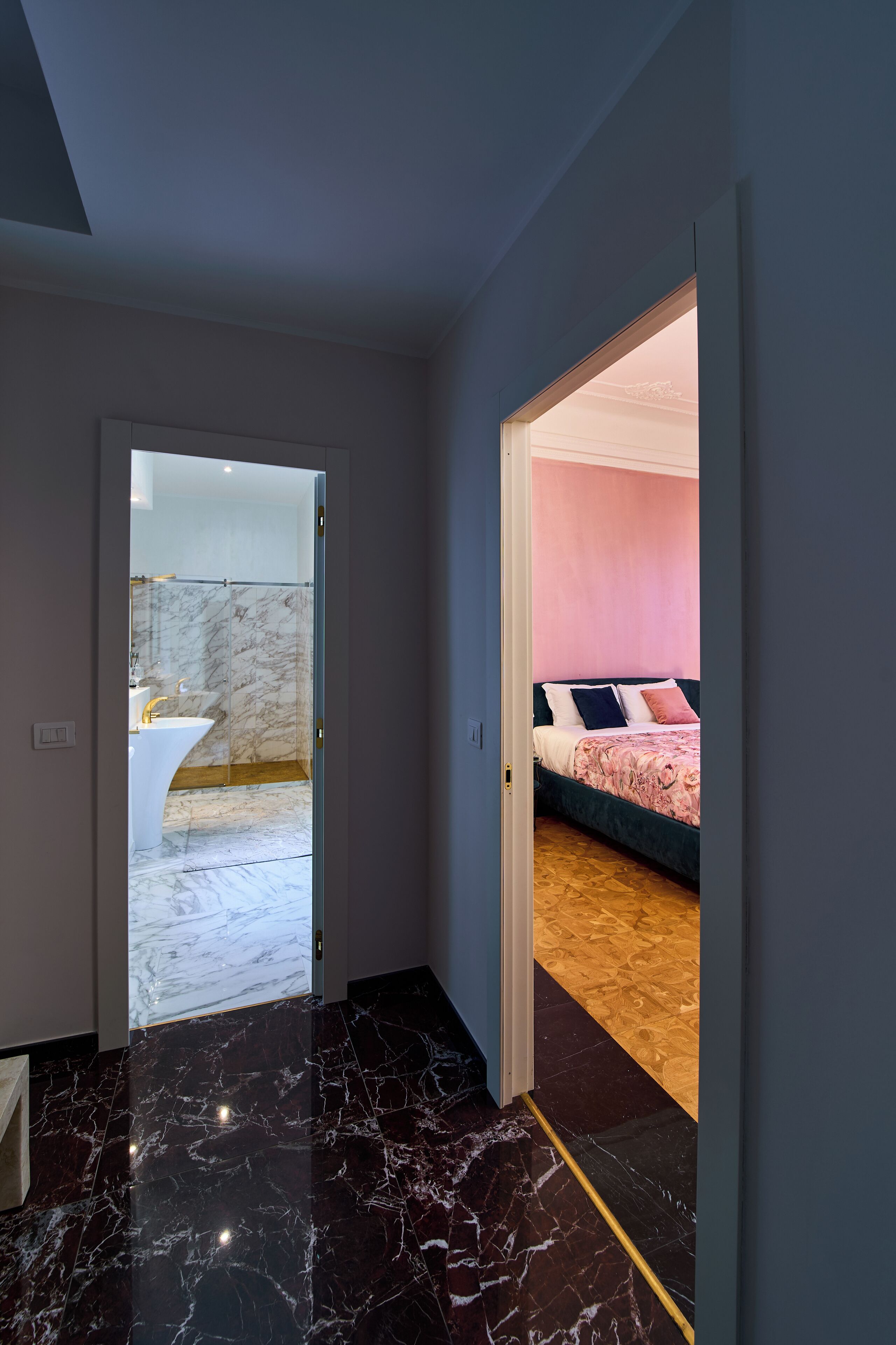 Quarto de hotel moderno com banheiro de mármore, cama com roupa de cama rosa e piso de madeira.