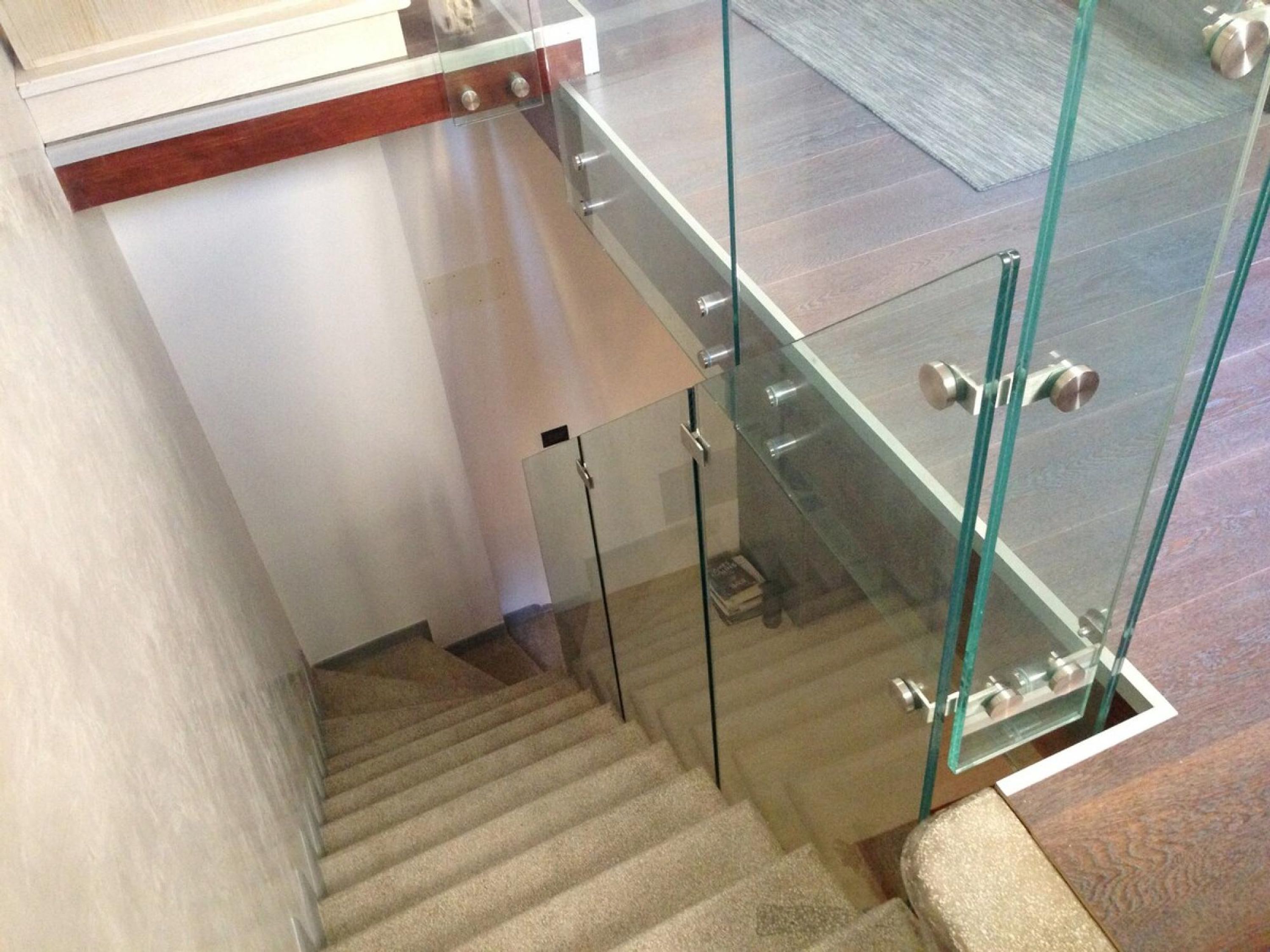 Escada com grades de vidro e detalhes em madeira nas paredes.