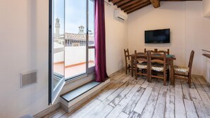 Quarto com varanda, mesa de jantar com cadeiras, televisão presa na parede e teto de madeira.