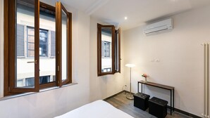 Quarto de hotel com cama, escrivaninha, abajur, espelho e ar condicionado.