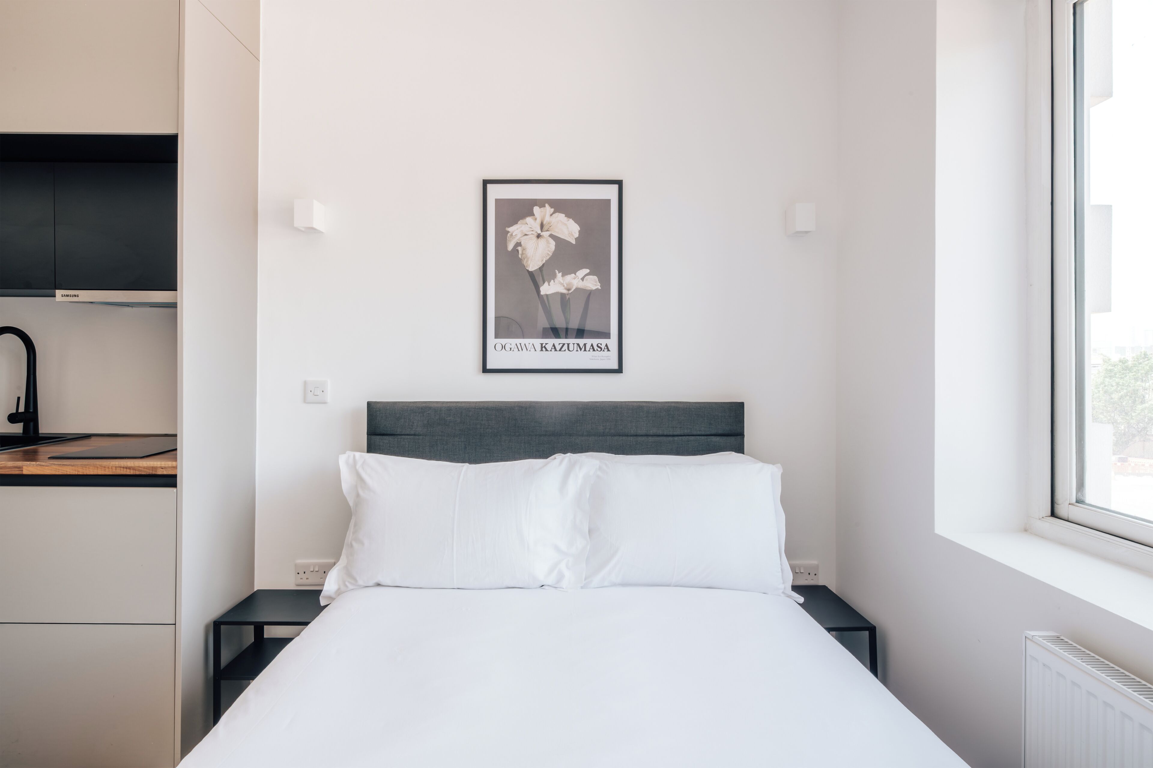 Quarto de hotel com uma cama, mesa de cabeceira, quadro na parede e uma janela.