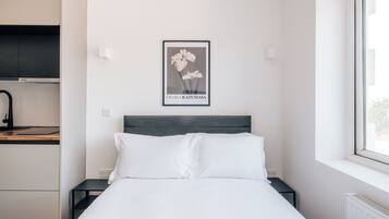 Quarto de hotel com uma cama, mesa de cabeceira, quadro na parede e uma janela.
