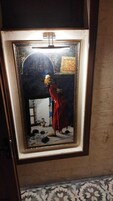 Obra emoldurada retratando uma pessoa vestida de vermelho, com piso de azulejos e uma pequena planta ao fundo.
