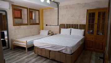 Quarto com duas camas de solteiro e uma cama de casal, piso de madeira, parede de tijolos e guarda-roupa de madeira.