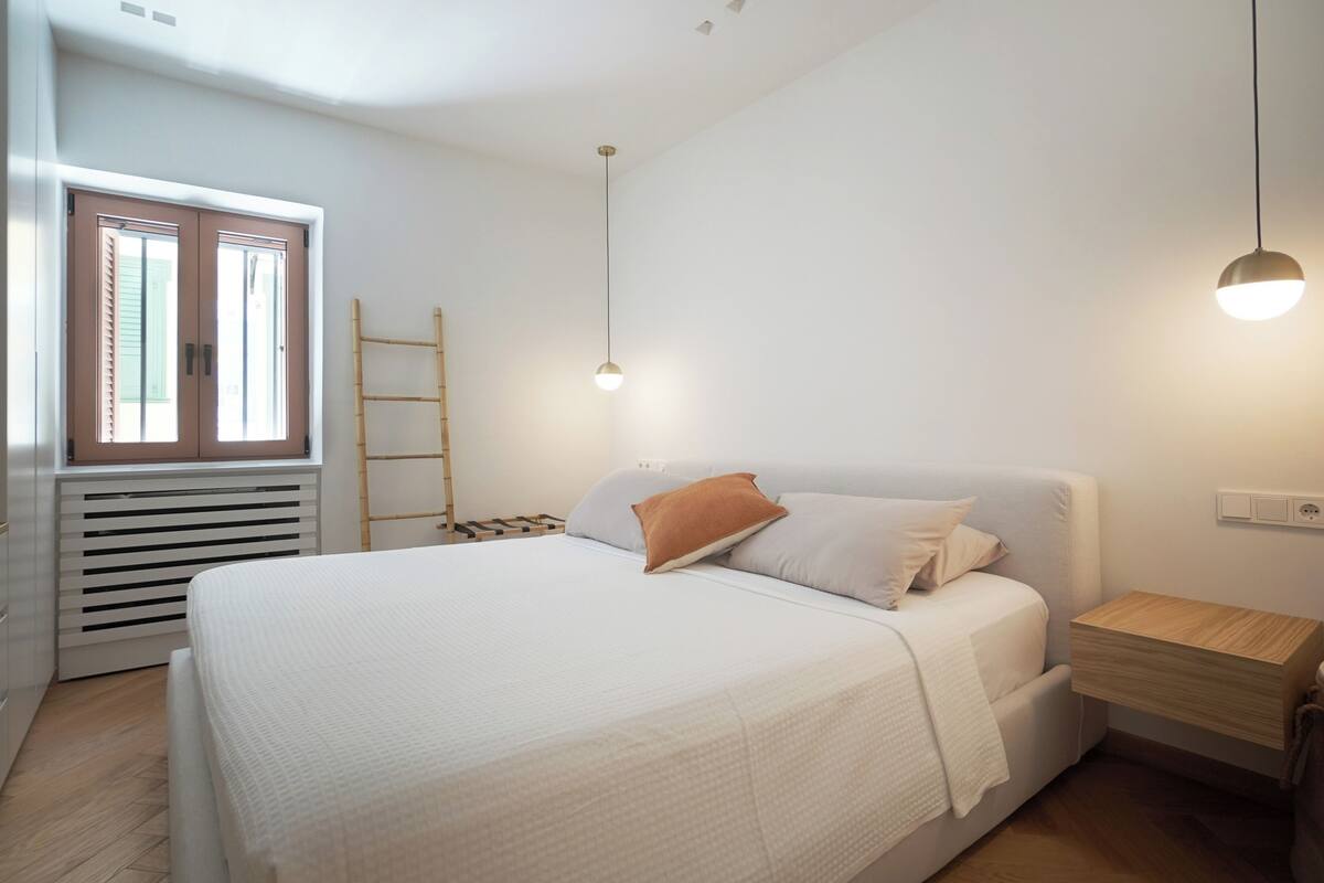 Quarto com cama, mesa de cabeceira, janela e escada.