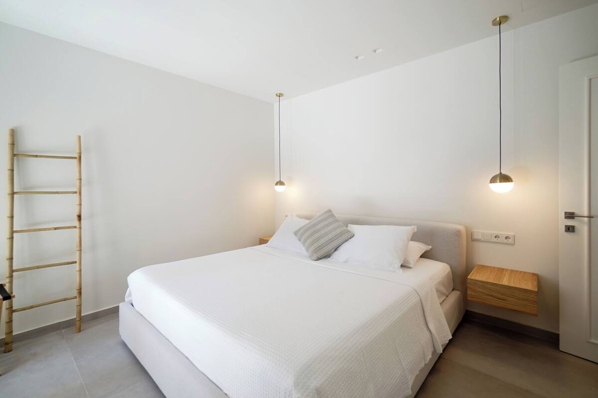 Quarto bem arrumado com cama, mesas de cabeceira e prateleira na parede.