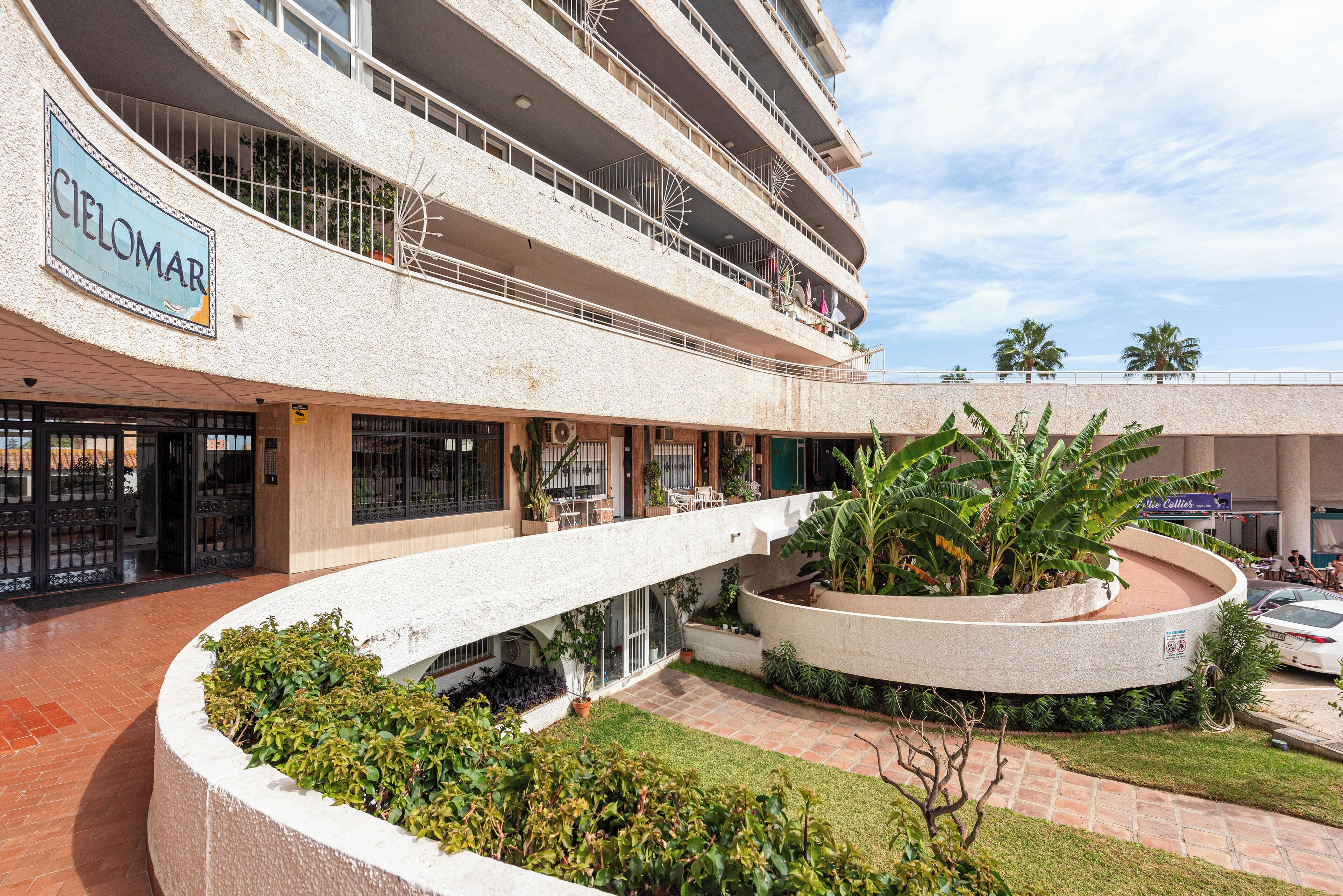Um hotel com vários andares, com uma placa que diz 'Cielomar' e uma área de jardim curva com plantas.