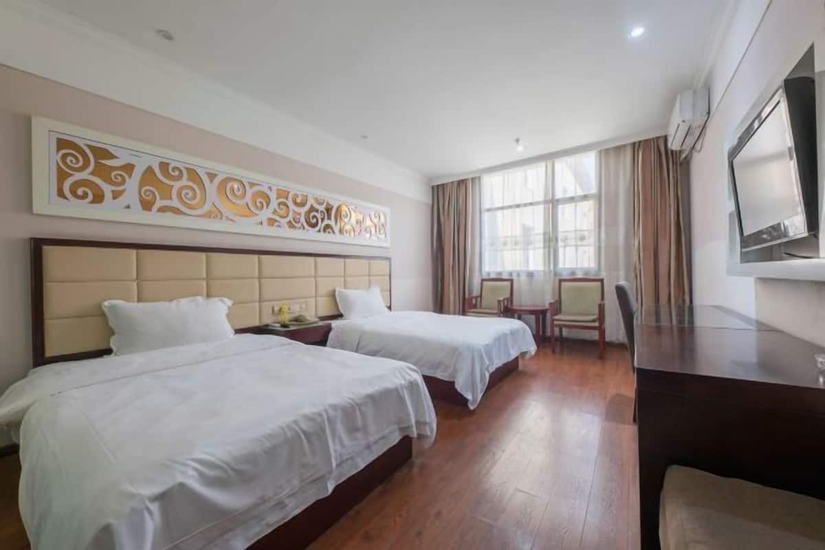 Quarto de hotel com duas camas, uma escrivaninha, uma cadeira e uma televisão.