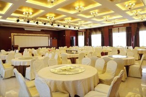 Salão de banquetes com mesas redondas, cadeiras brancas e lustres.