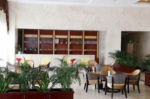 Um saguão com piso de mármore, área de estar com cadeiras, estante com diversos objetos e plantas em vasos.