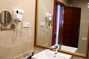 Casa de banho com um espelho grande, uma pia e dois secadores de cabelo fixados na parede.