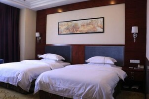 Quarto de hotel com duas camas, um quadro na parede e uma mesa de cabeceira com abajur.