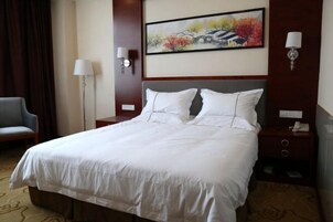 Quarto de hotel com uma cama grande, duas mesas de cabeceira, uma cadeira e um quadro na parede.
