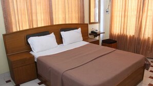 Uma cama de solteiro com cabeceira de madeira, duas almofadas, uma mesinha de cabeceira e um criado-mudo.