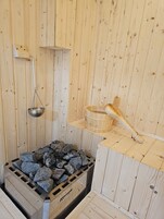 Uma sauna com paredes de madeira, um banco de pedra, uma bacia de metal e uma concha de madeira.