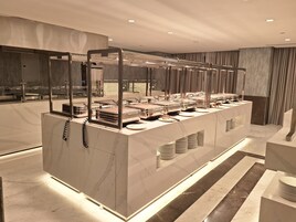 Disposição moderna de buffet com bancada de mármore, eletrodomésticos de aço inoxidável e estrutura de vidro.