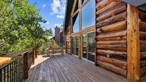 Um deck de madeira com um banco, janelas amplas e vista para as árvores.