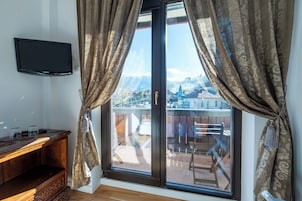 Quarto com porta de vidro deslizante para uma varanda, televisão de tela plana na parede e mesa de cabeceira de madeira com copos.