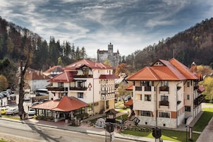 Uma cidade europeia tradicional com edifícios de telhados vermelhos, uma praça central e um castelo ao fundo.