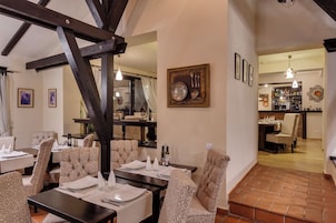 Uma sala de jantar com vigas de madeira, cadeiras estampadas e piso de tijolos.