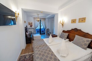 Quarto de hotel com uma cama grande, cabeceira de madeira, um candelabro e vista para o quarto vizinho.