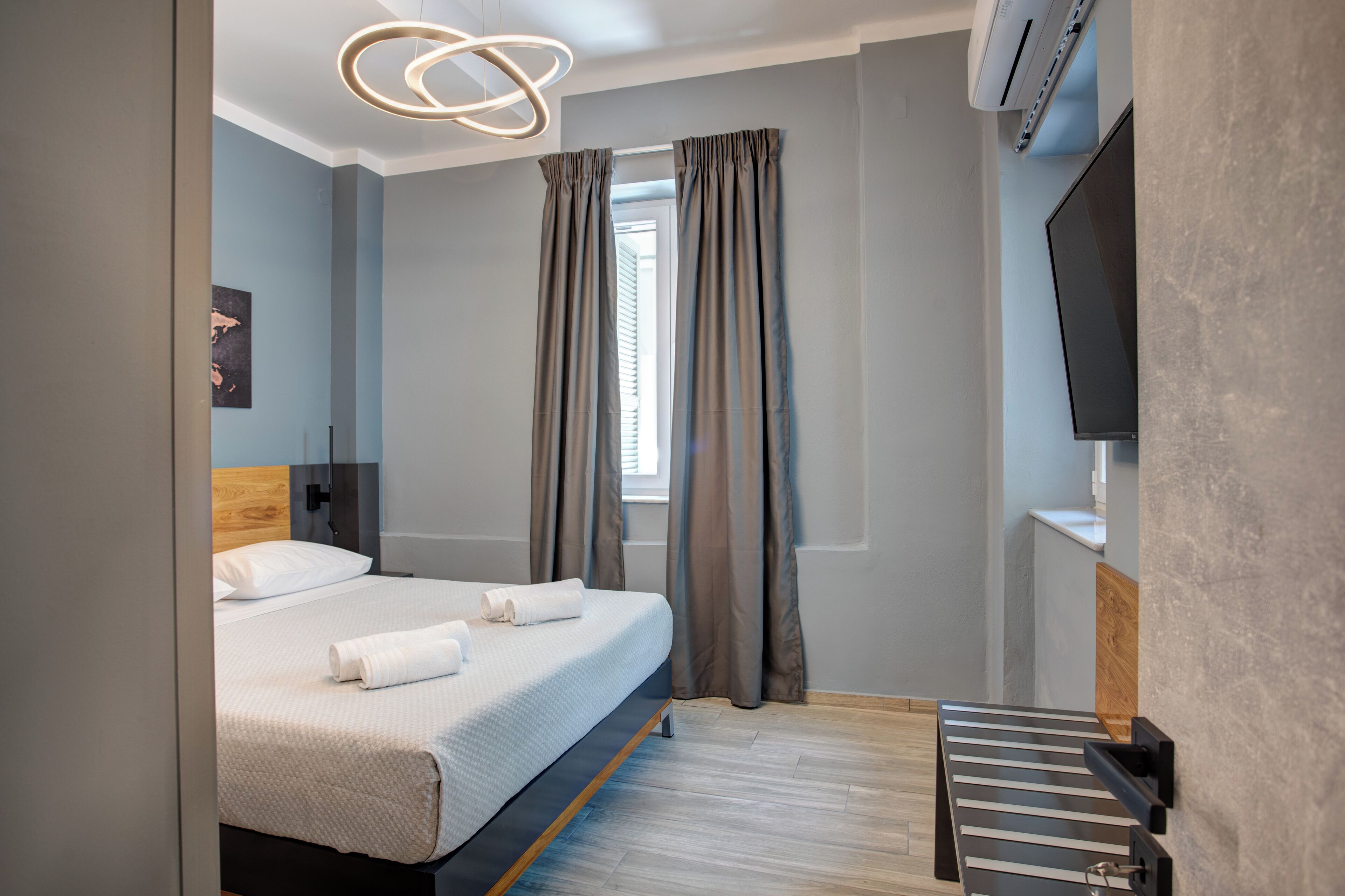 Quarto de hotel moderno com cama, televisão e janela com cortinas.