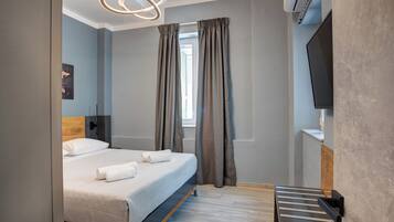Quarto de hotel moderno com cama, televisão e janela com cortinas.