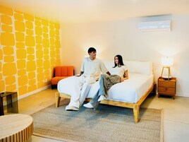 Quarto com cama, mesa de cabeceira, luminária, cadeira e parede com padrão geométrico.