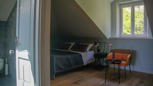 Um quarto com teto inclinado, uma cama, uma cadeira e uma janela.