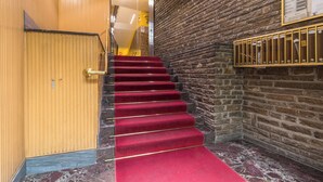 Uma escadaria com carpete vermelho, uma porta de madeira e uma parede de pedra.