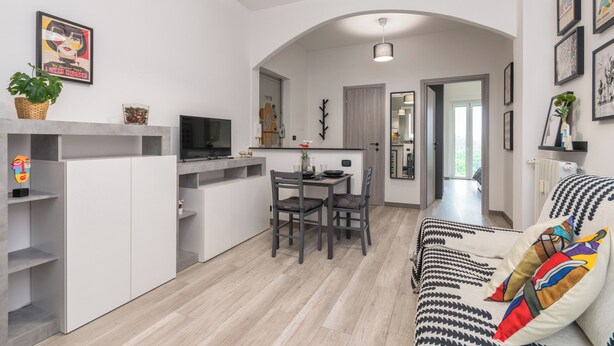 Uma sala de estar moderna com sofá, área de jantar com mesa e cadeiras, cozinha com televisão e corredor que leva a outro quarto.