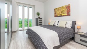 Quarto moderno com uma cama grande, uma mesa de cabeceira, uma planta em vaso e um quadro na parede.
