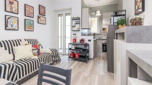 Uma sala de estar moderna com um sofá, uma mesa de centro e um espaço de jantar com uma mesa e cadeiras. Há uma cozinha com geladeira, pia e bancada.