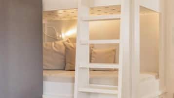 Uma cama beliche com escada, um banco e uma mesinha.